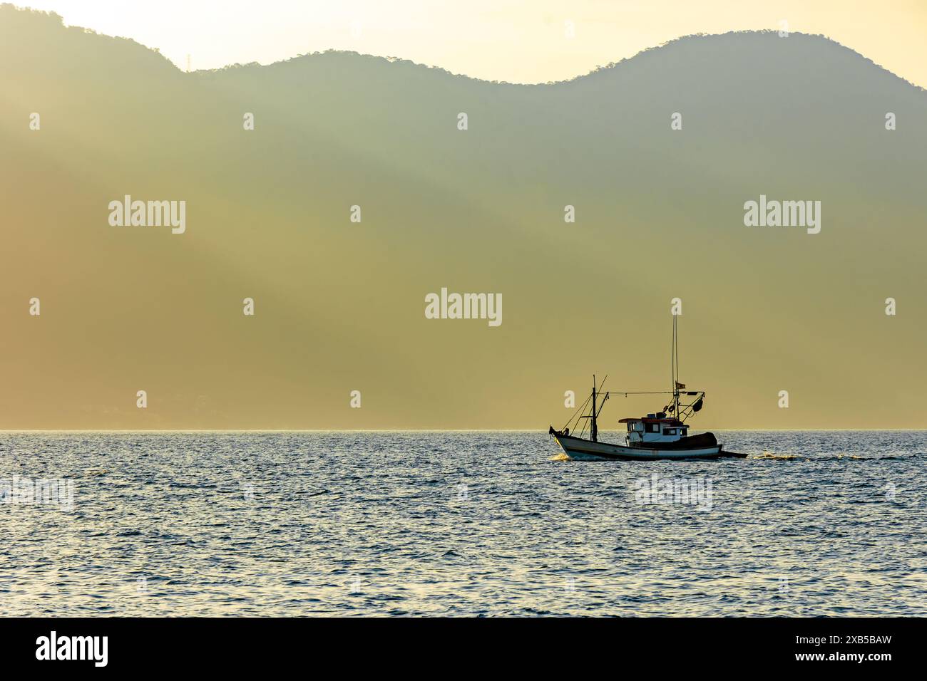 Fishing trawler sailing in front of the mountains of Ilhabela during ...
