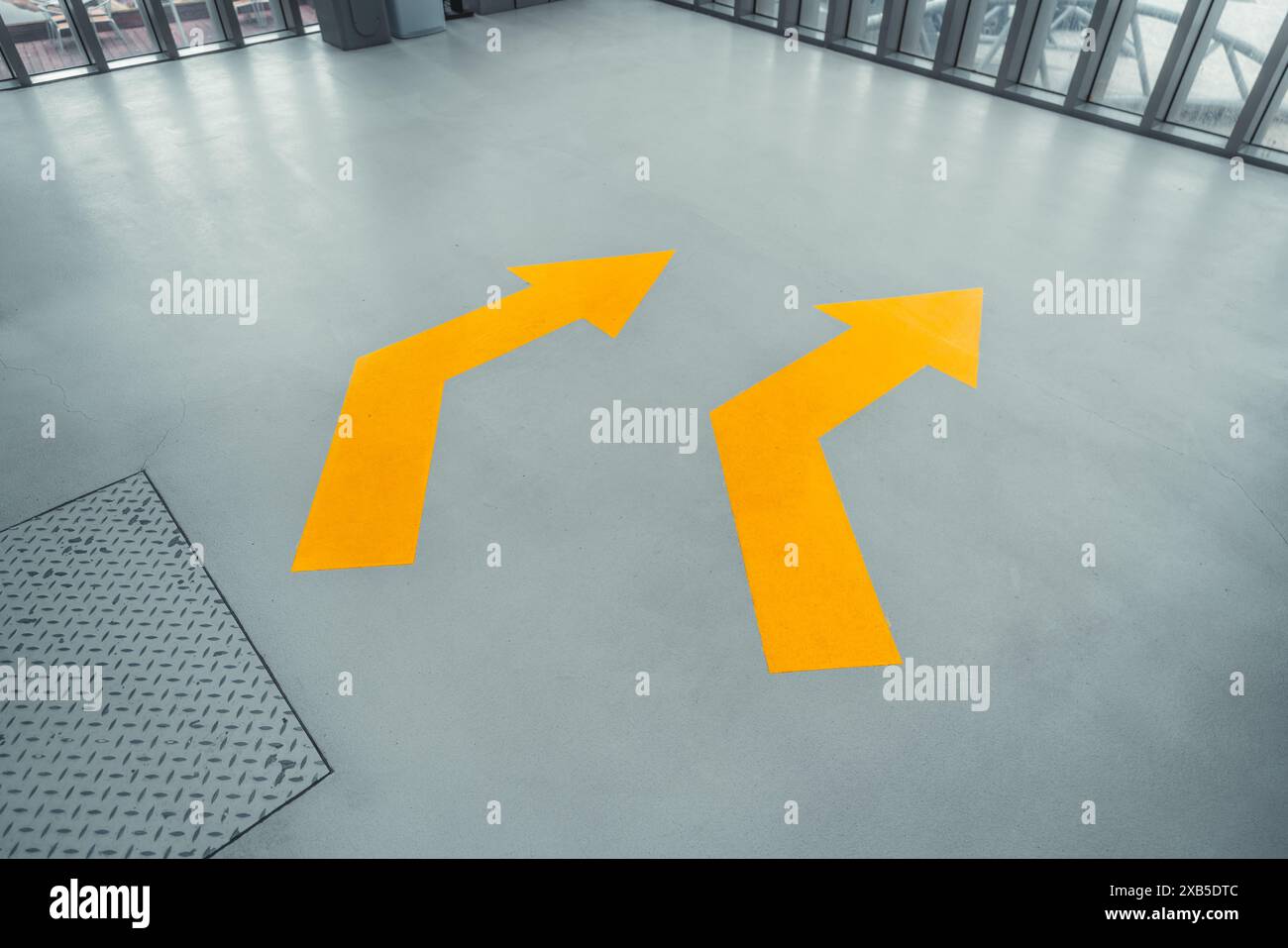 Two bright yellow arrows painted on a gray concrete floor, indicating ...