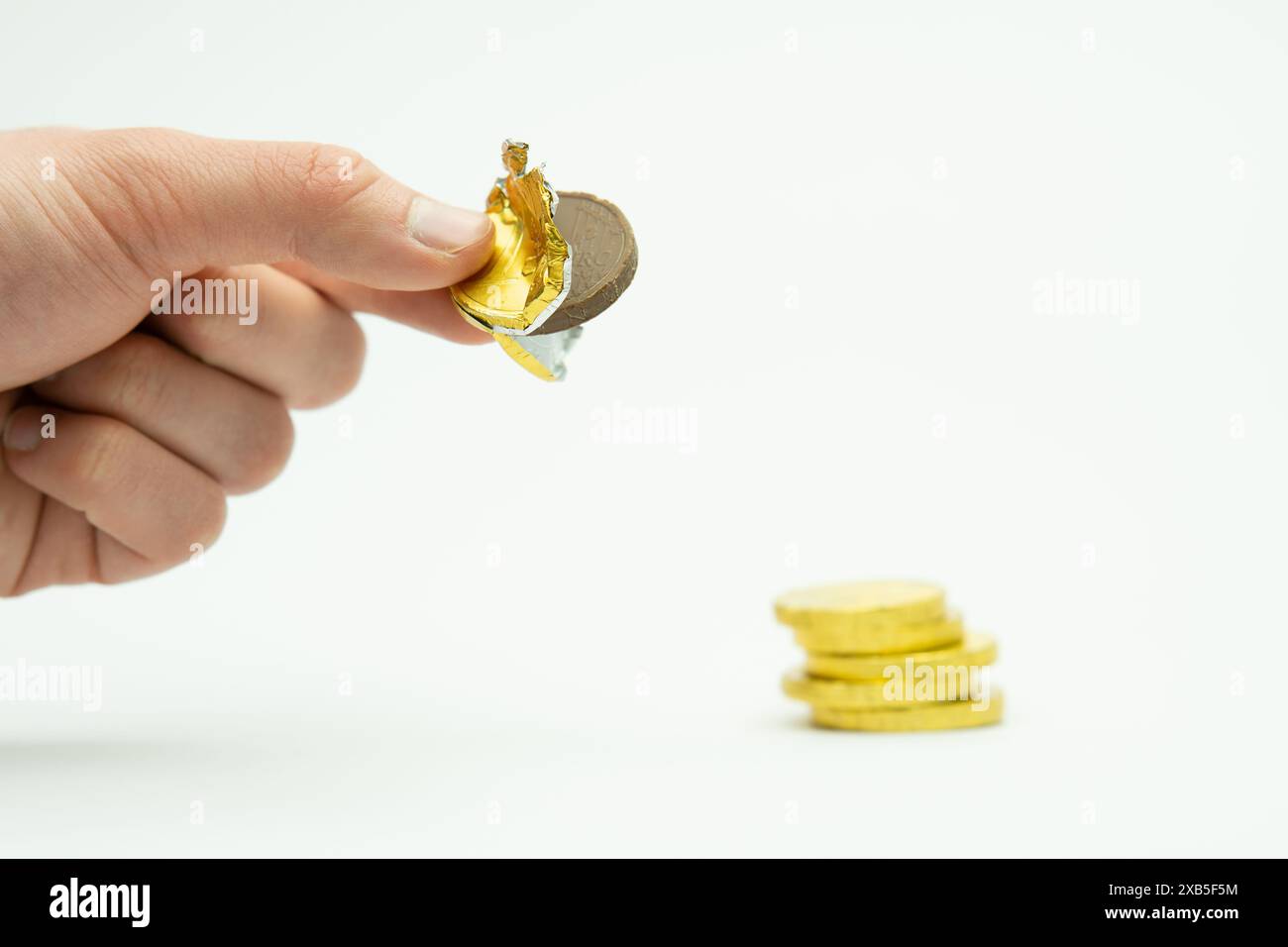 Male hand holding chocolate coin, stack of coins in the background ...