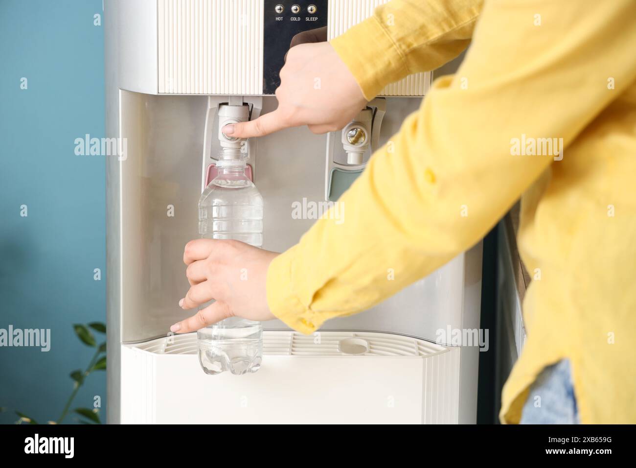 Woman filling plastic bottle with filtered water from cooler near blue ...