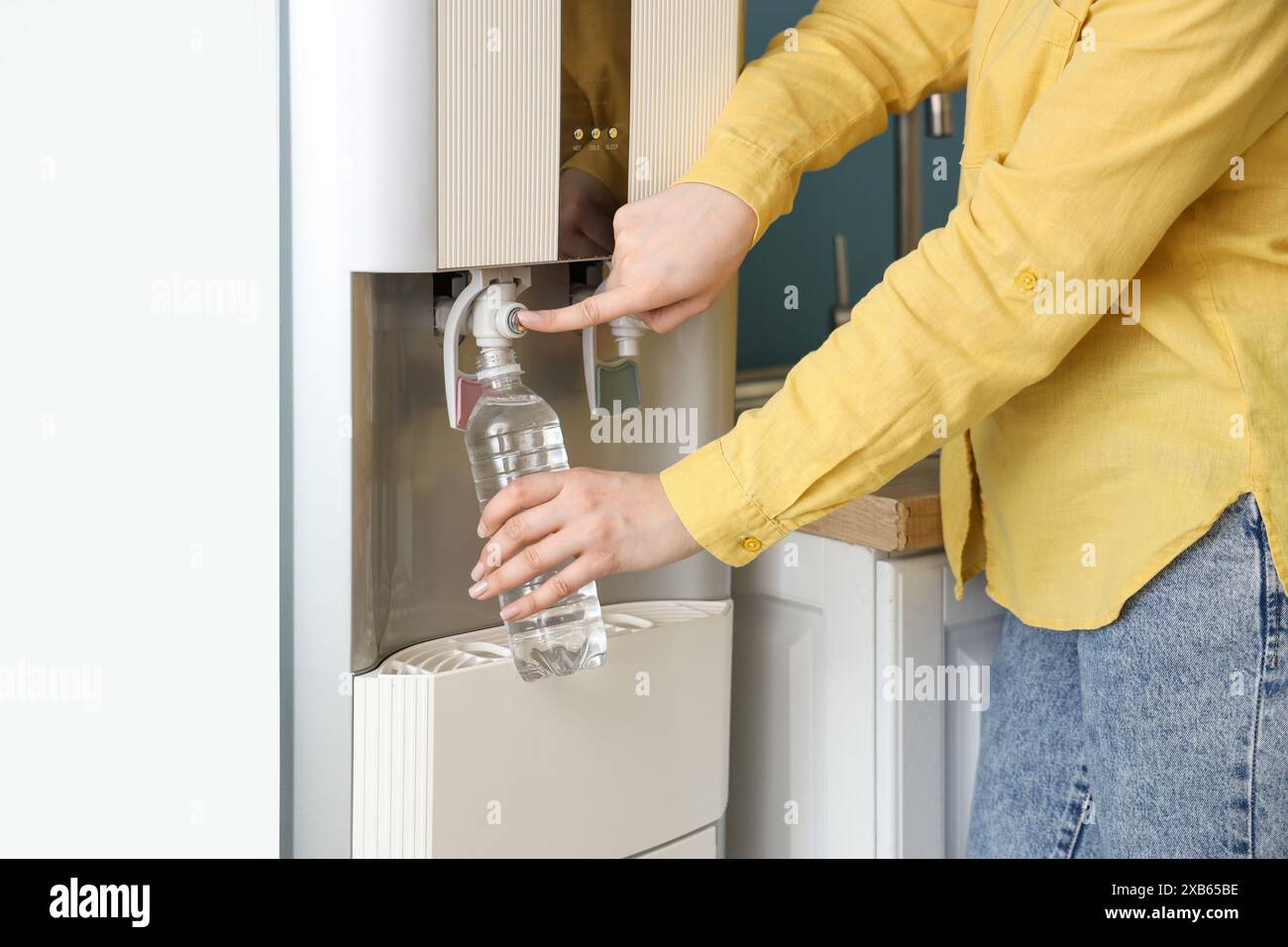 Woman filling plastic bottle with filtered water from cooler near blue ...