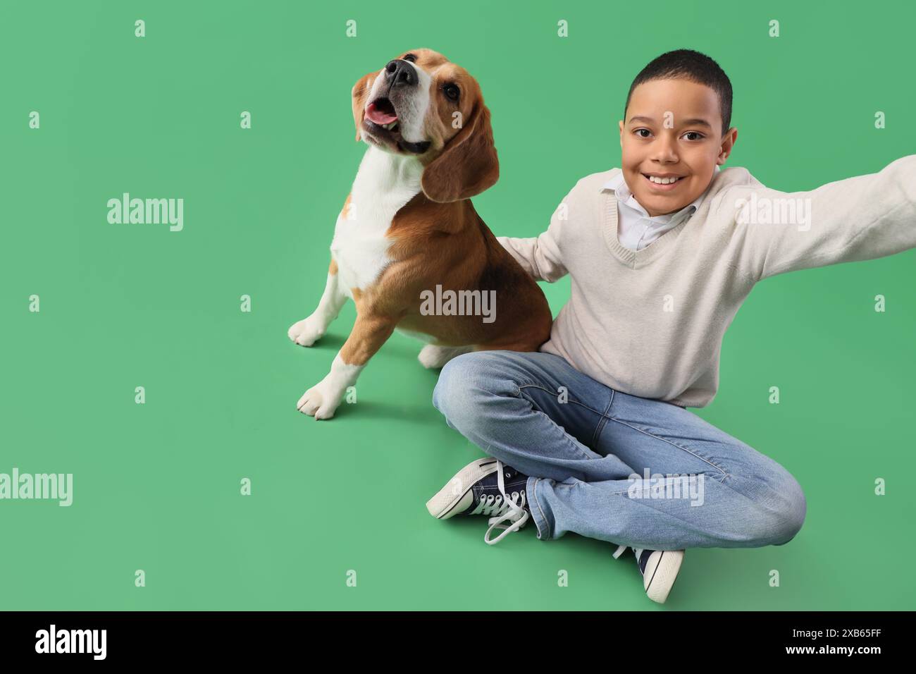 Little African-American boy with cute beagle dog on green background ...