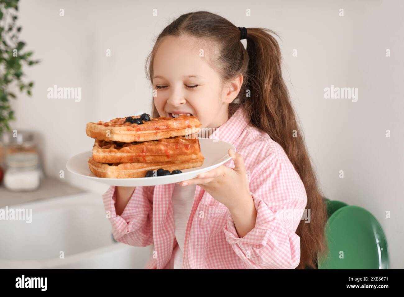 Cute little girl eating waffles with honey in kitchen Stock Photo - Alamy