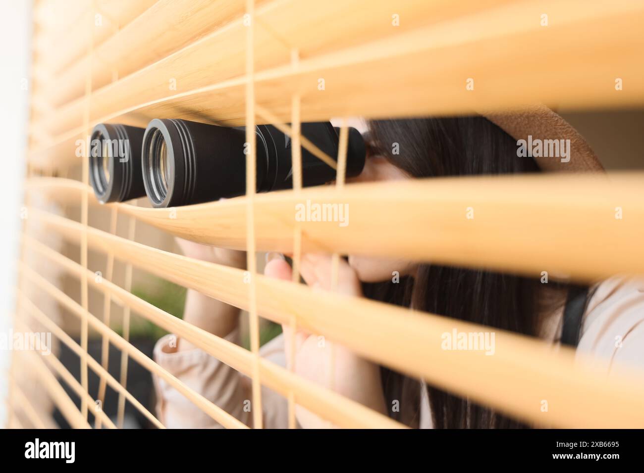 Female spy looking through binoculars near window in office, closeup ...