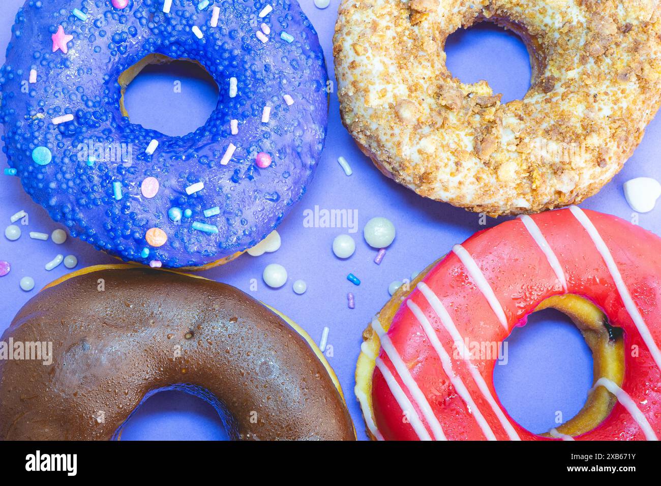 Four donuts with a different topping laying down on a blue background ...