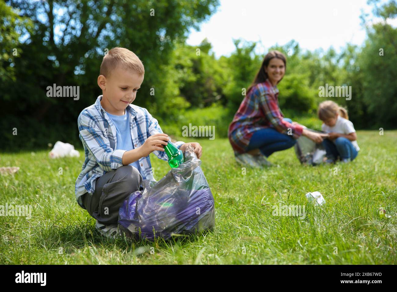 Mother and her children with plastic bags collecting garbage in park ...