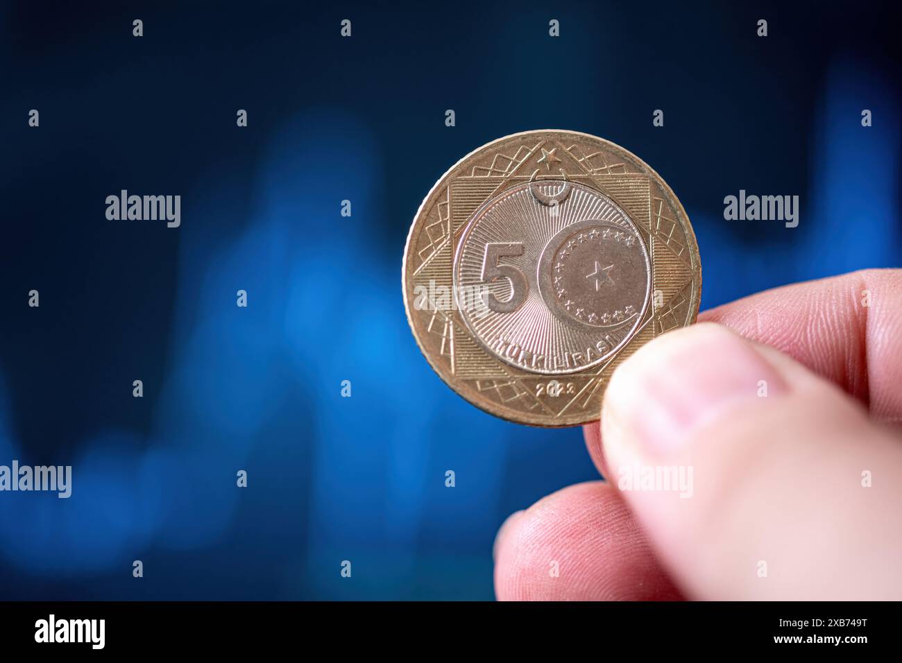 Hand holding a 5 Turkish Lira coin in front of a screen with financial ...