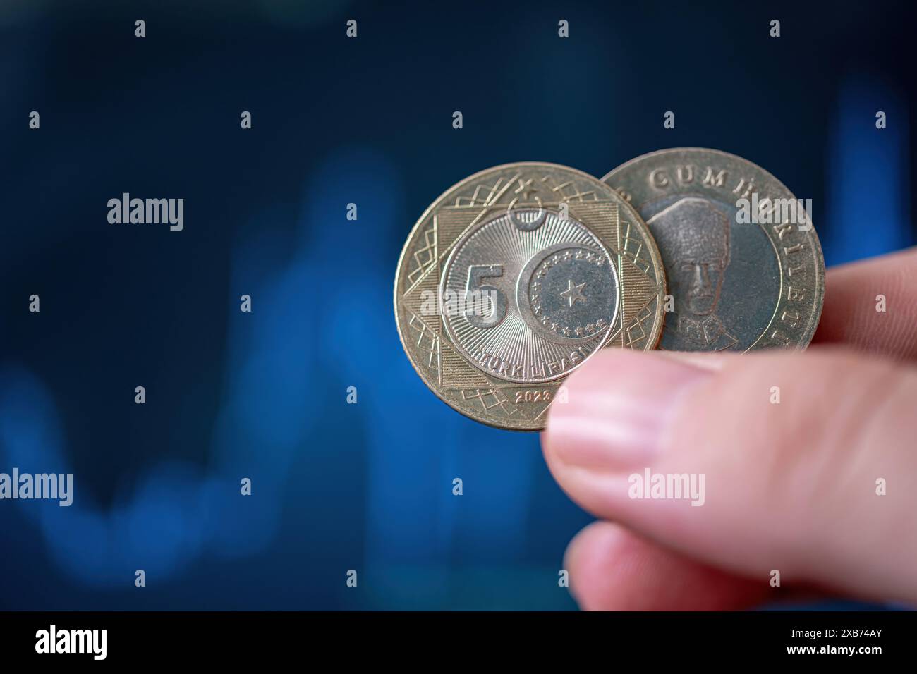Hand holding a 5 Turkish Lira coin in front of a screen with financial ...
