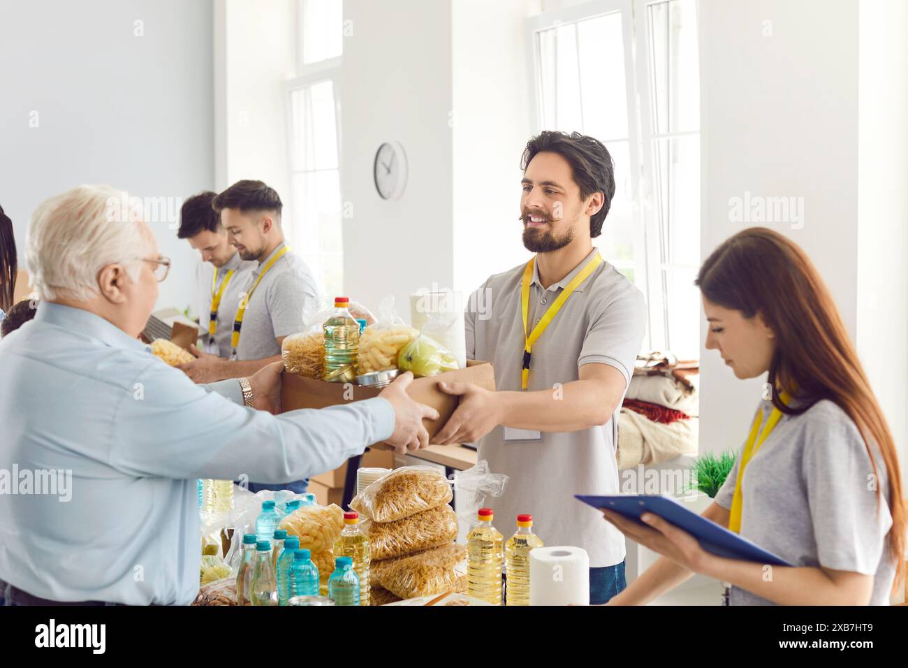 Helpful volunteers at a charity center give a poor senior man a box ...