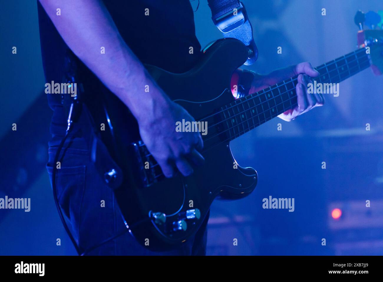 Electric bass guitar player is in blue stage lights, closeup photo with ...