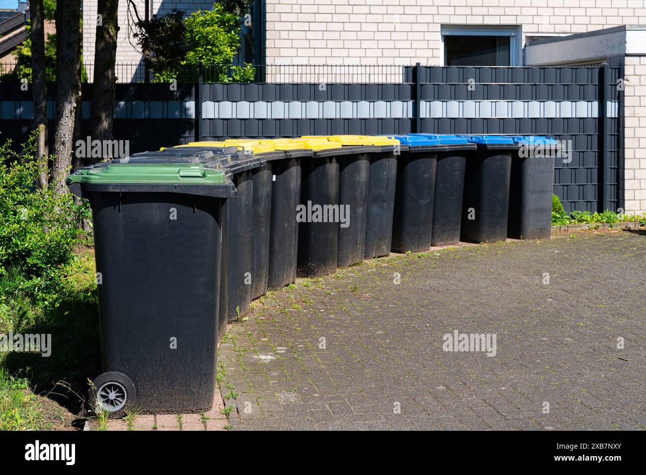 Plastic bins for separate waste collection are lined along the fence of ...