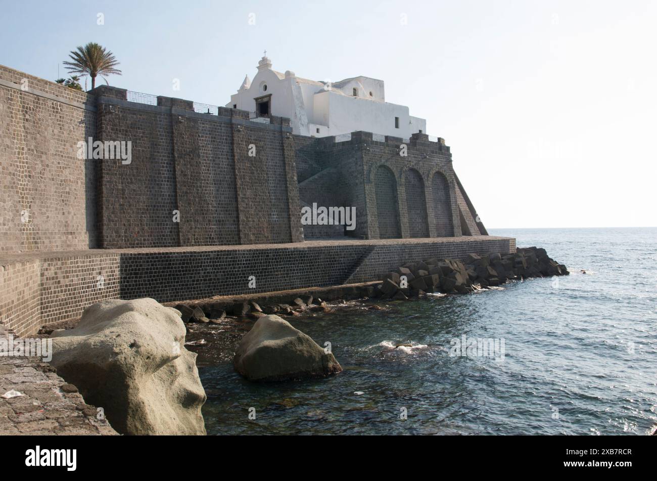 A rock formation near water next to building wall with cross Stock ...
