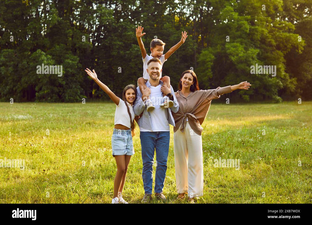Happy mom, dad and children standing on green grass in the park, waving ...