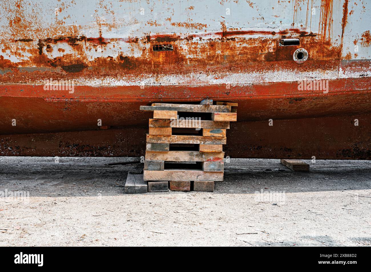 Weathered, rusty boats hull on wooden pallets on sandy ground ...