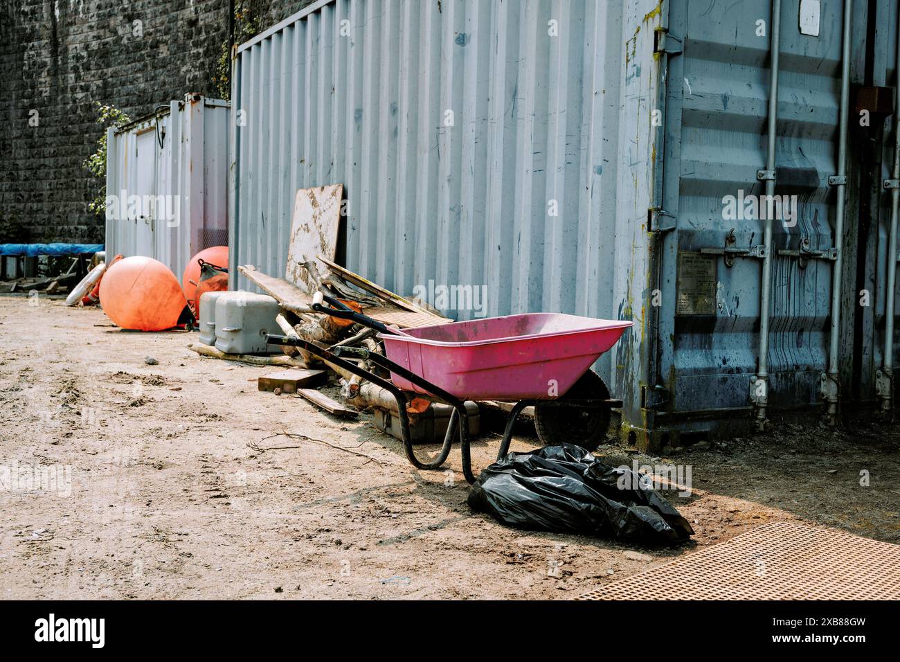 Pink wheelbarrow and construction materials near storage containers in ...