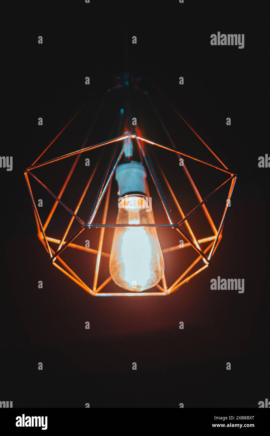 A glowing orange light bulb inside a suspended cage in a dim room Stock ...