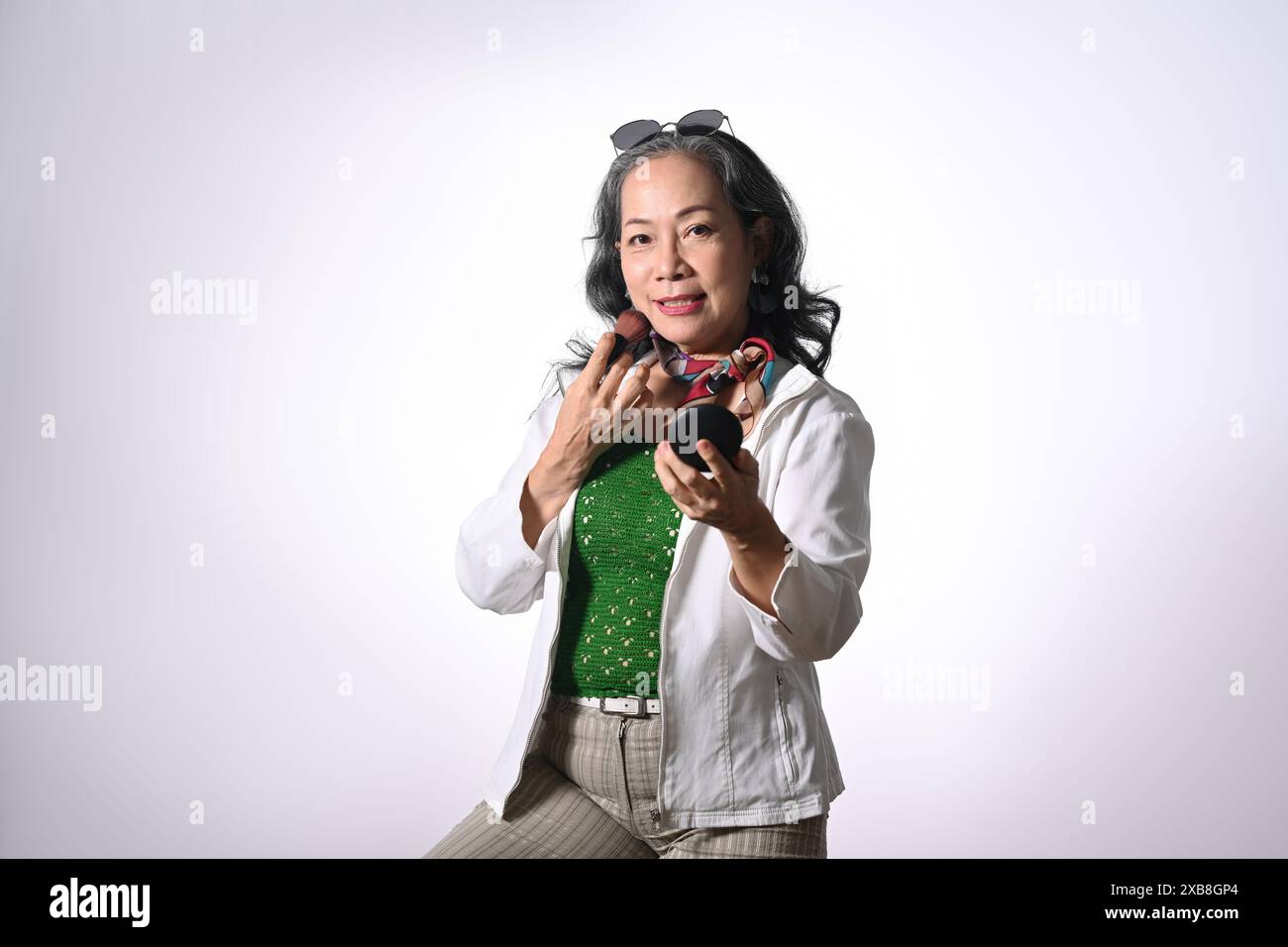 Charming senior lady applying face powder with brush isolated over ...