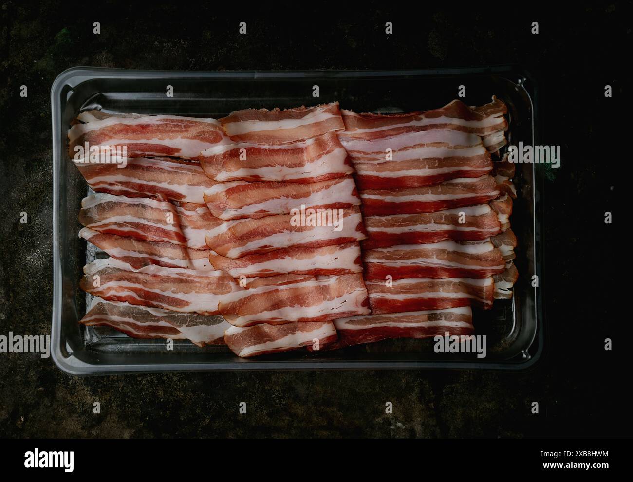 Thinly sliced bacon neatly arranged in a plastic tray. The strips ...