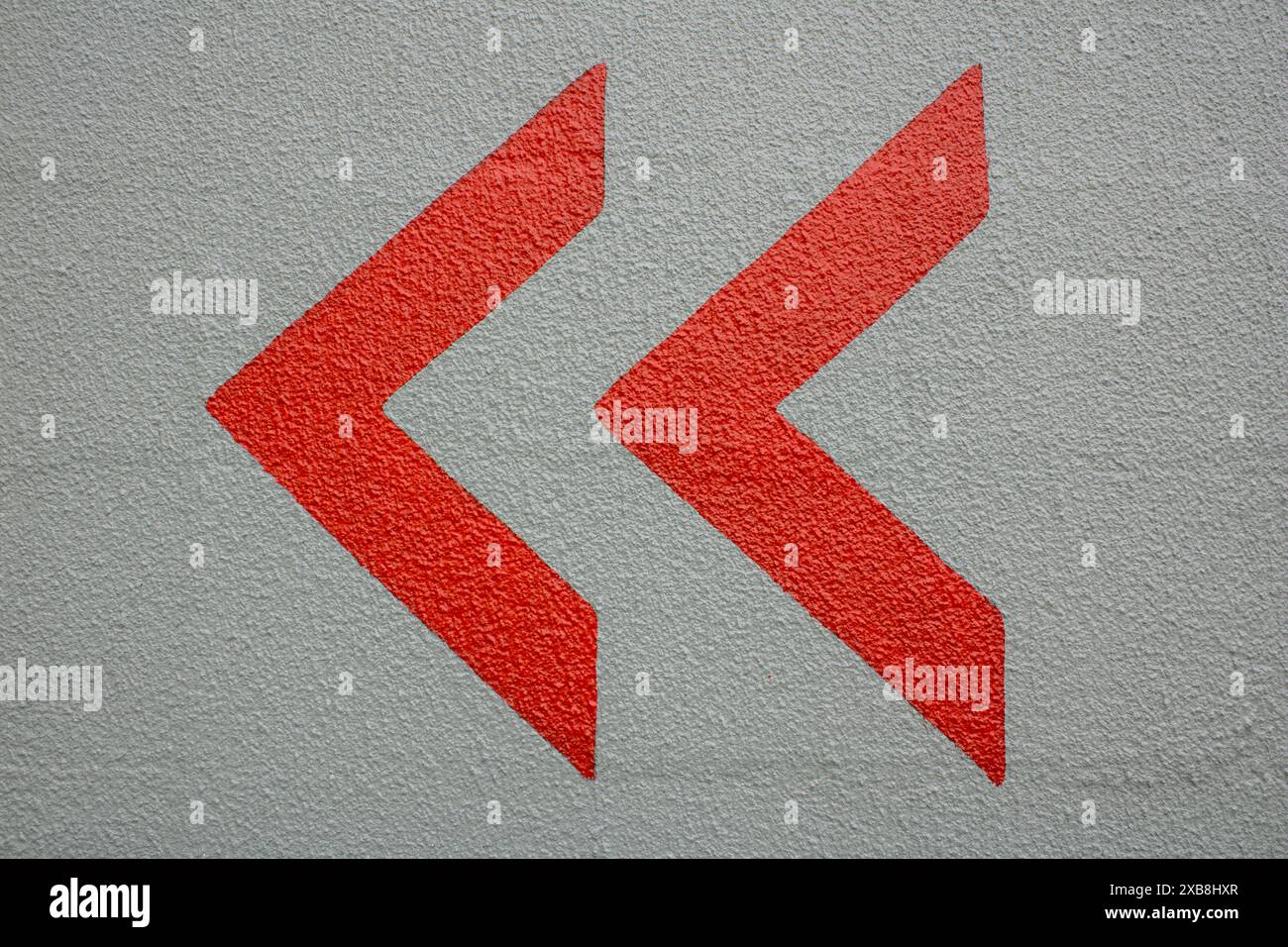 A gray wall with two red less-than signs Stock Photo - Alamy
