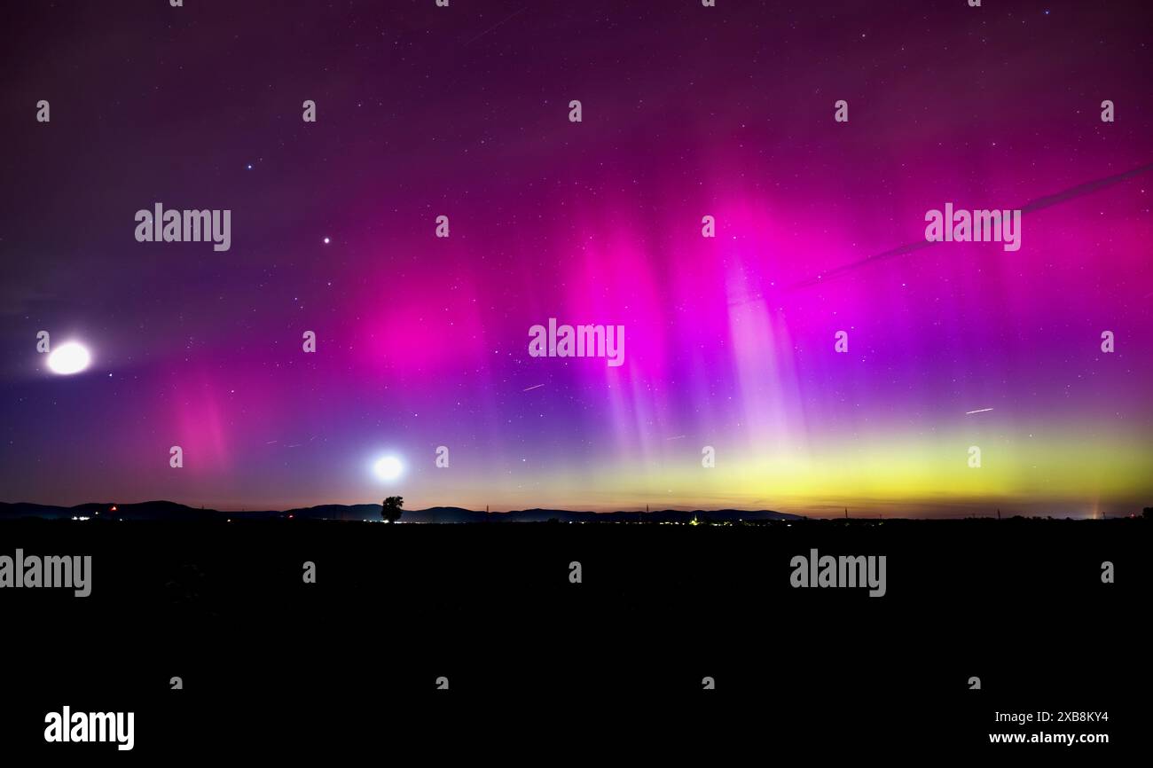 The Aurora borealis illuminating field at night with moon and small dot ...