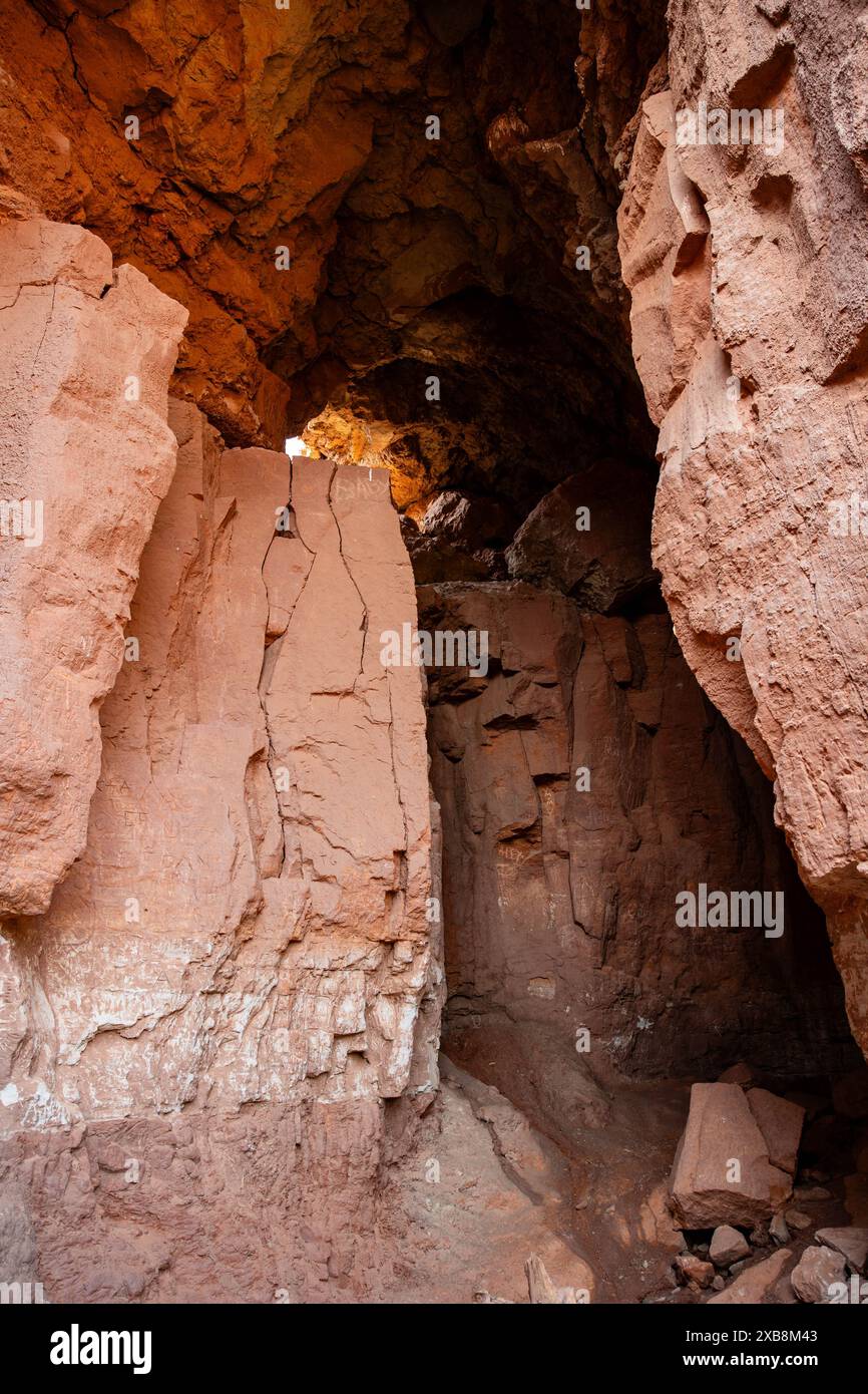 A cave with red rocks, small entrance, and a glowing light within Stock ...
