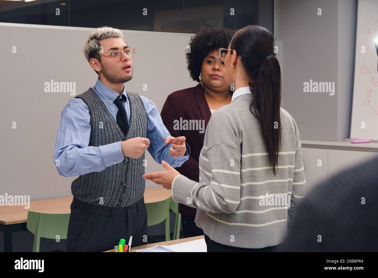 A Man and tow Women are standing in a meeting room, the man is ...