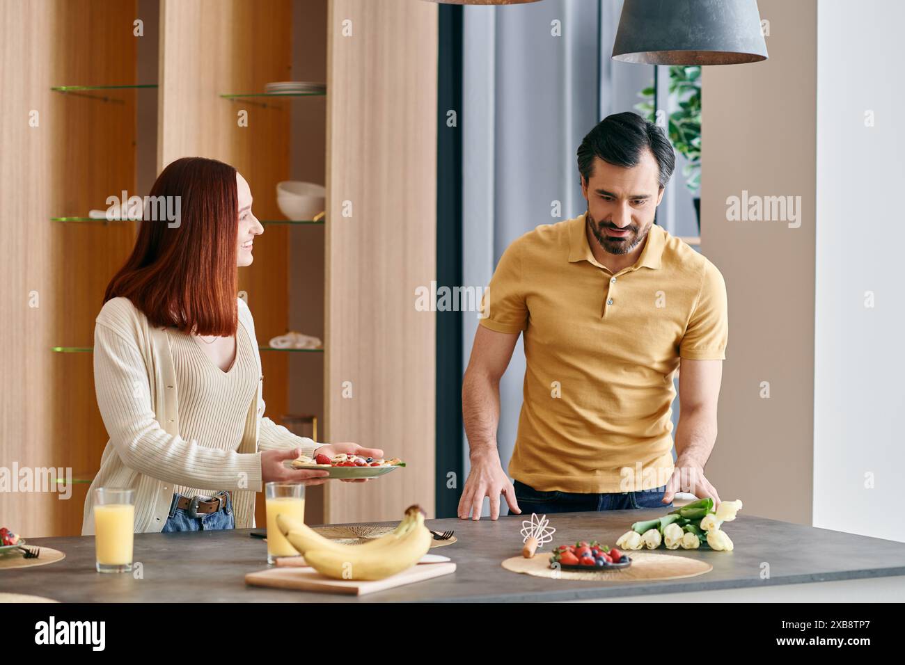 A redhead woman and bearded man cook together in a modern kitchen ...