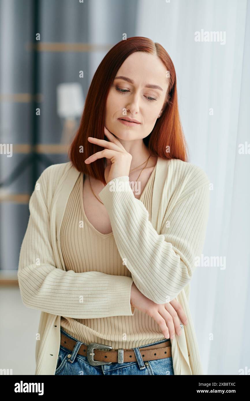 A red-haired woman stands gracefully in front of a window, the sunlight ...