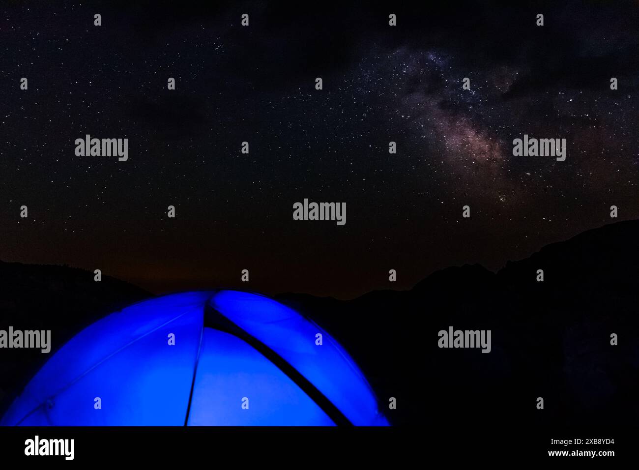 A glowing blue tent under a starry night sky in Retezat National Park ...