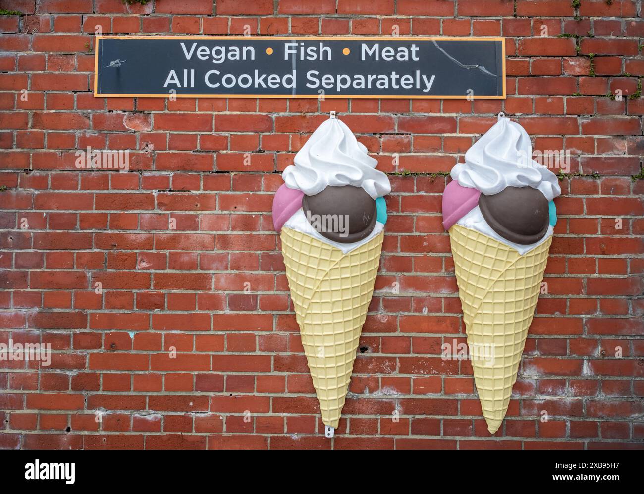Two giant ice cream cones fixed to a wall under a sign reading "Vegan ...