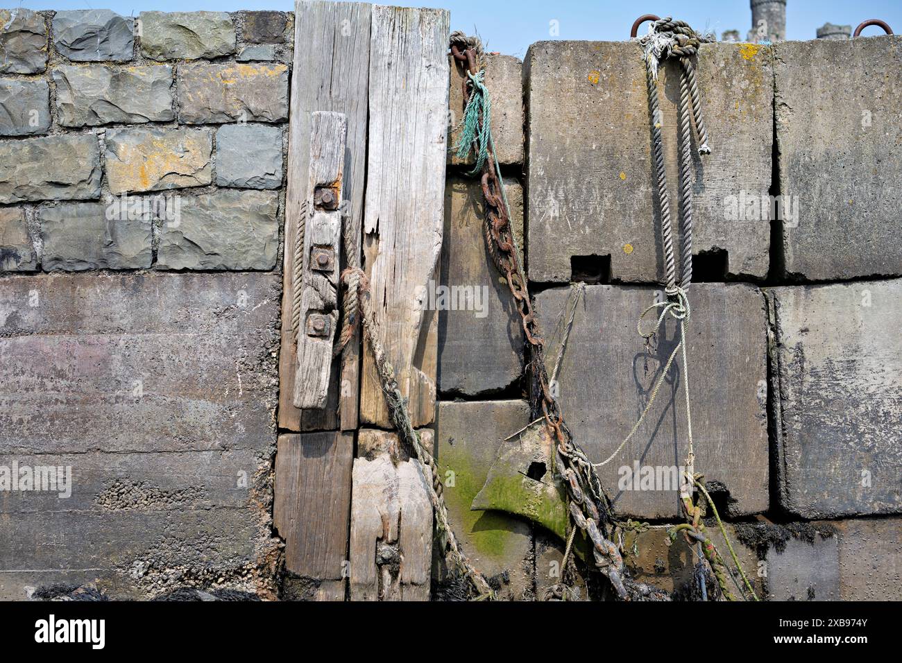 A rustic weathered old seawall with aged wood, stone, chains, and ropes ...