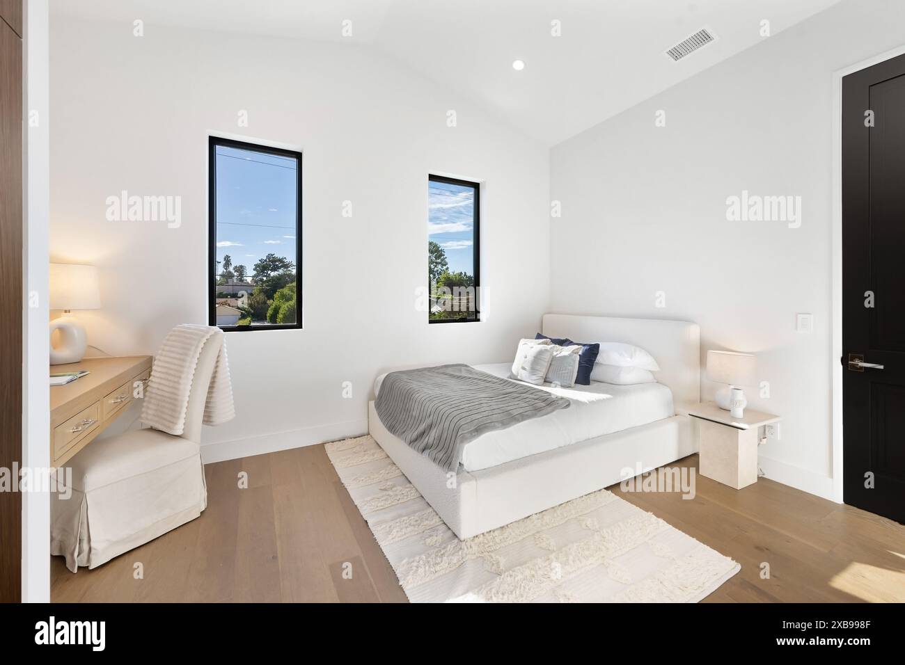 A modern bedroom with a bed and desk positioned by a window Stock Photo ...