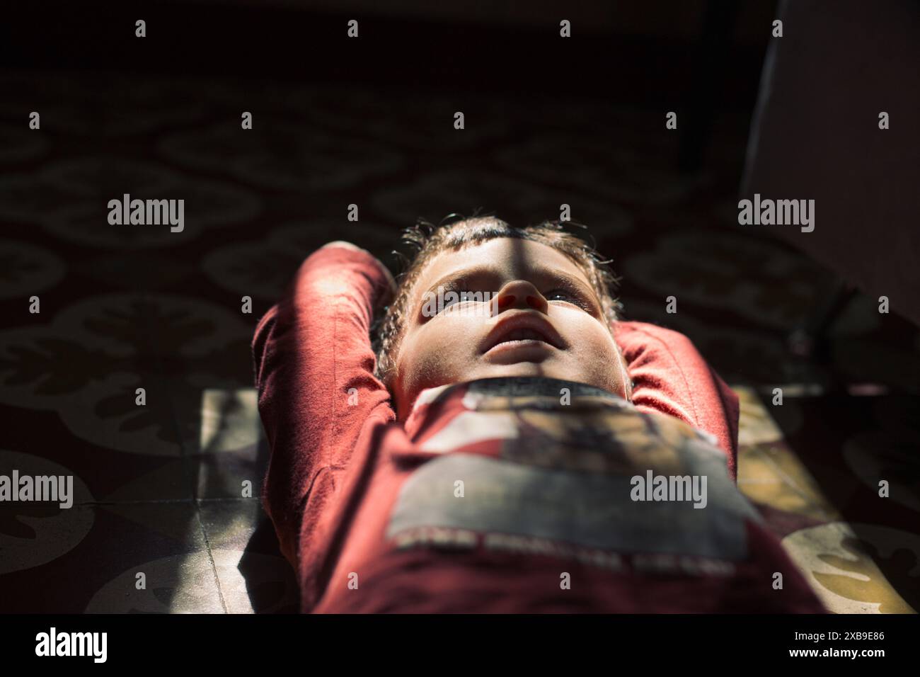 A young child lying on the floor with sunlight casting shadows on their ...