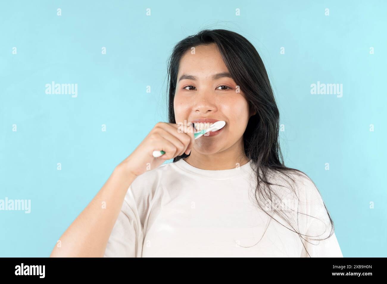 A woman is brushing her teeth with a green toothbrush. She has a smile ...