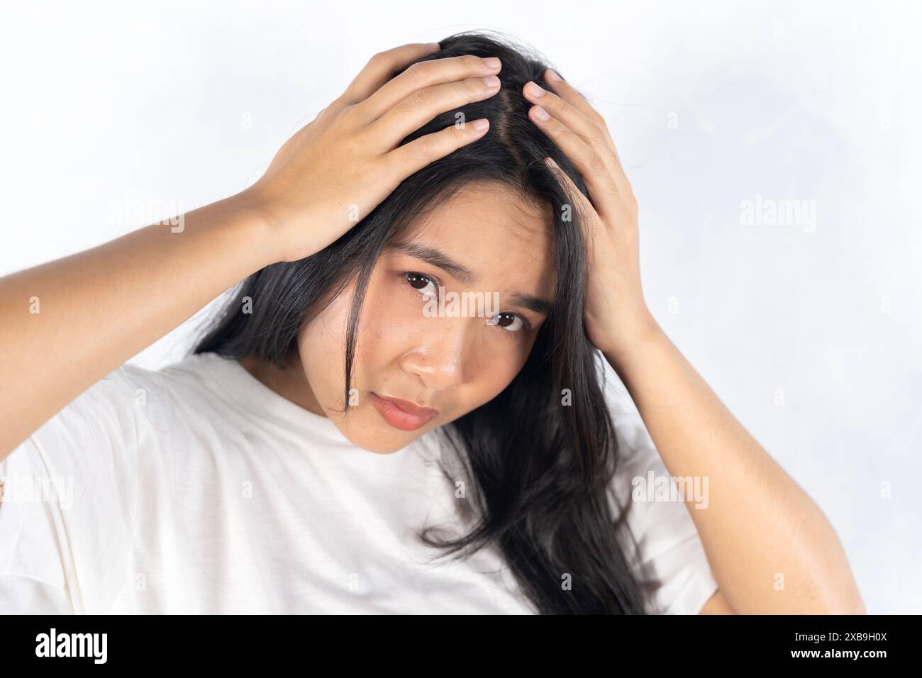 A woman with her hands on her head, looking sad. She is wearing a white ...