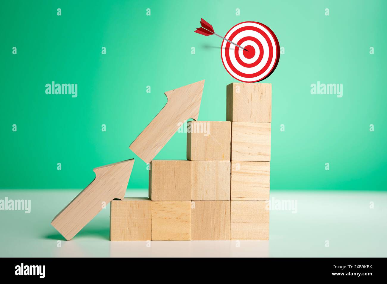 Target icon on top of wooden blocks with rise up arrows, 3d bar graph chart steps on green ...