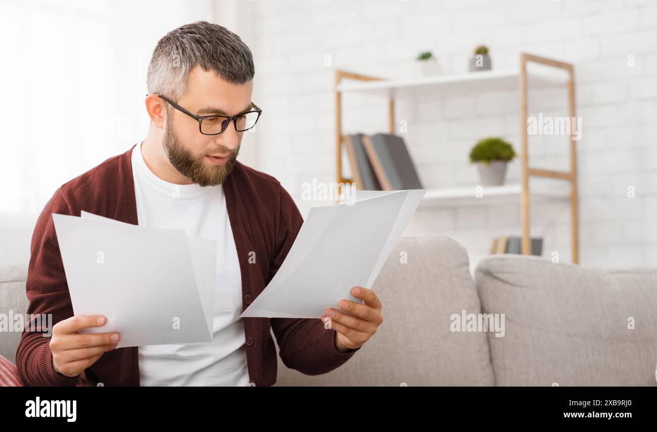 Man Sitting on Couch Reading Piece of Paper Stock Photo - Alamy