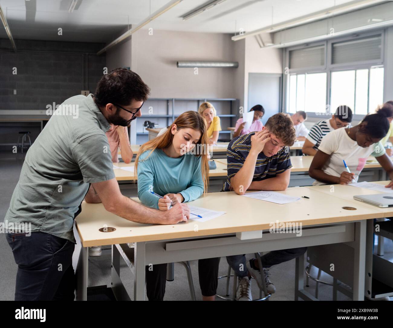 Male teacher advising a group of diverse students in class. High school ...