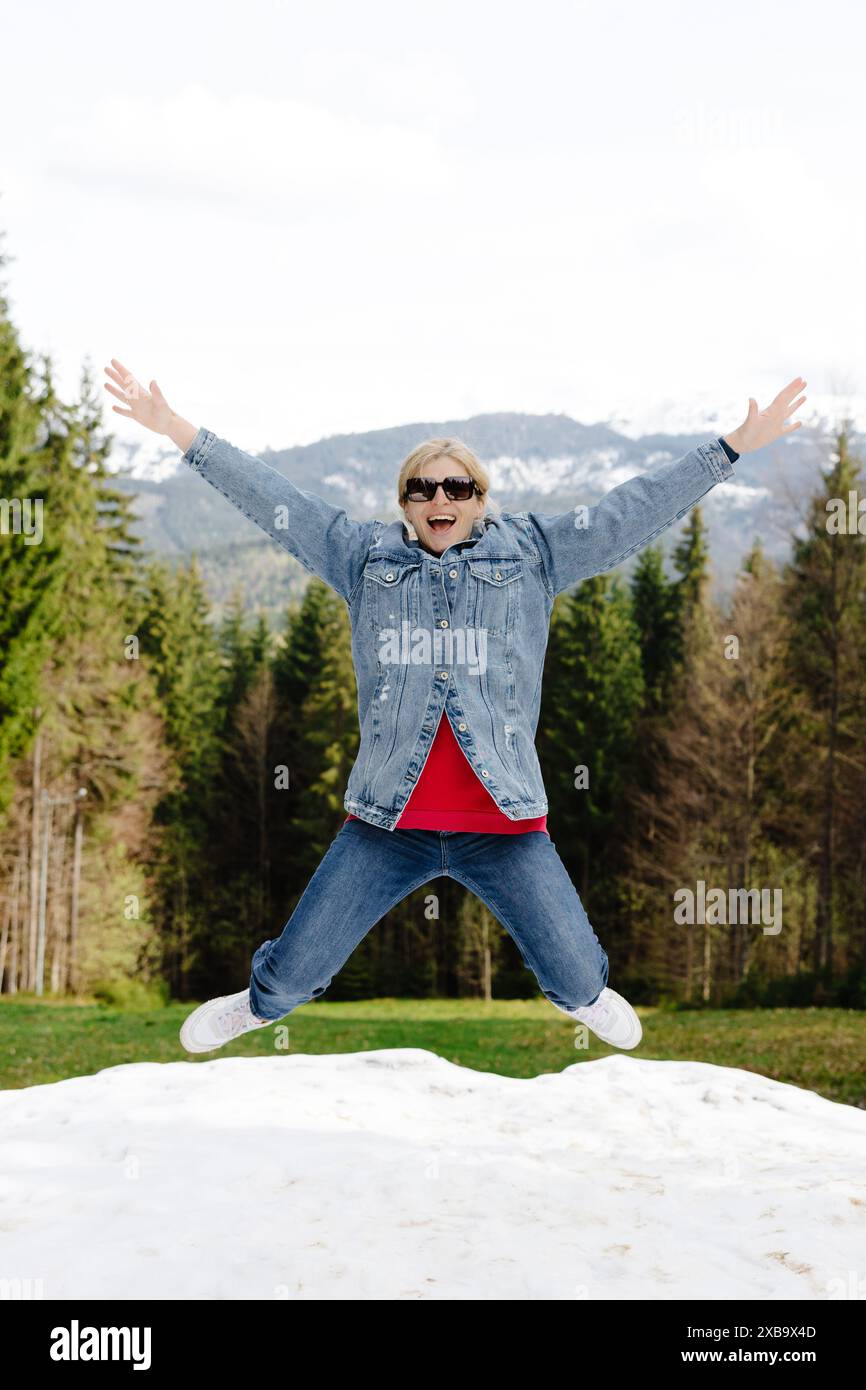 A woman wearing a blue denim jacket and jeans jumps in the air, arms ...
