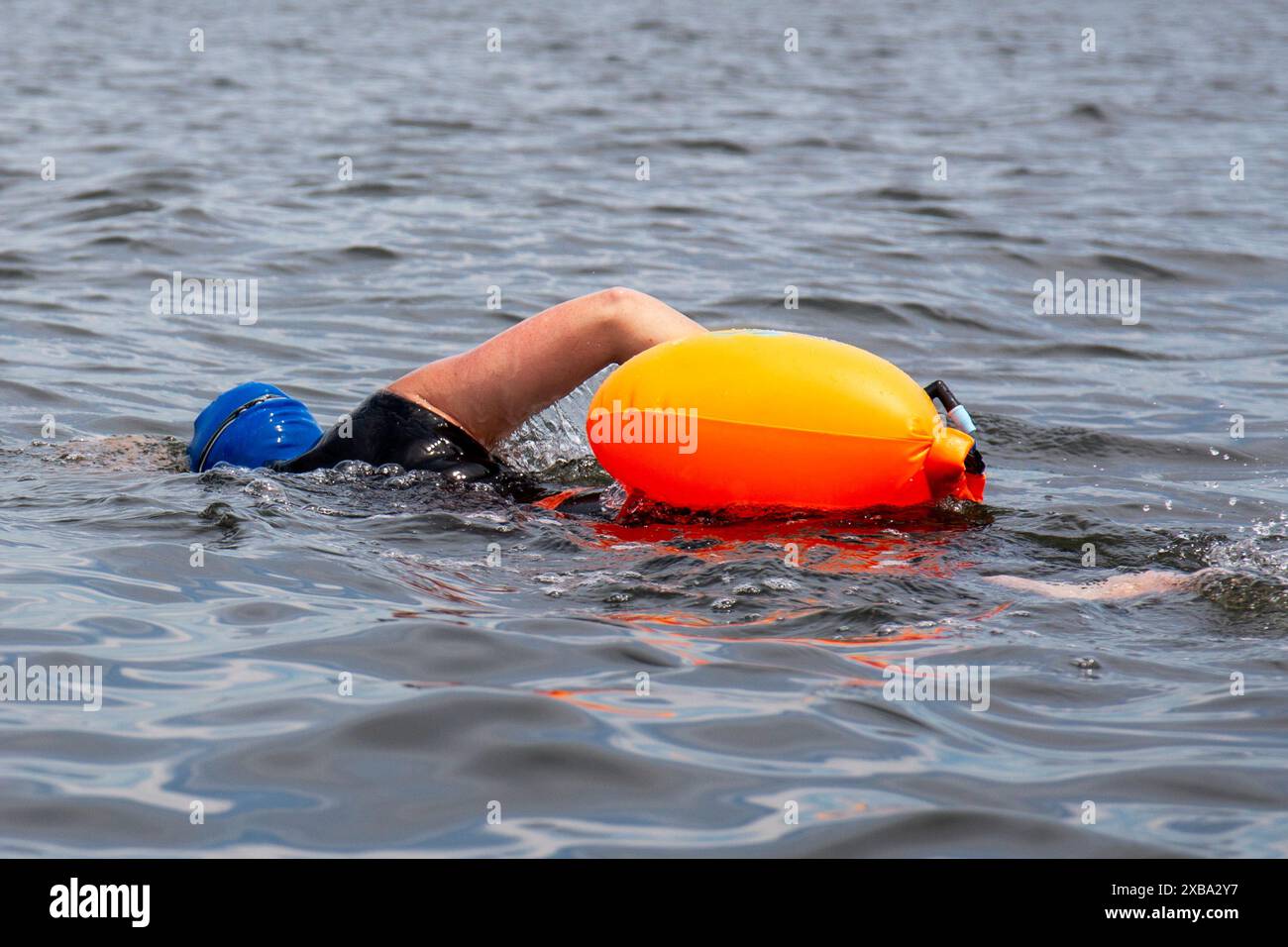 Close up of one female swimming wearing an orange safety floatation device in open water alone ...