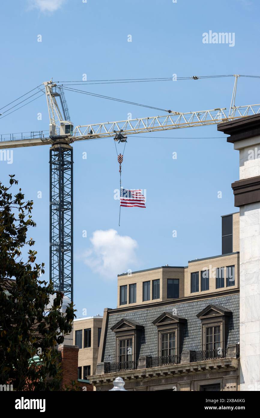A construction crane hoisting an American flag above a city building ...