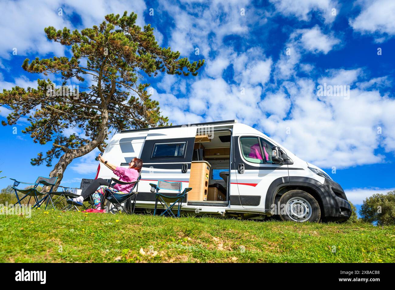 Woman sitting in front of campervan or motorhome parked on the beach ...