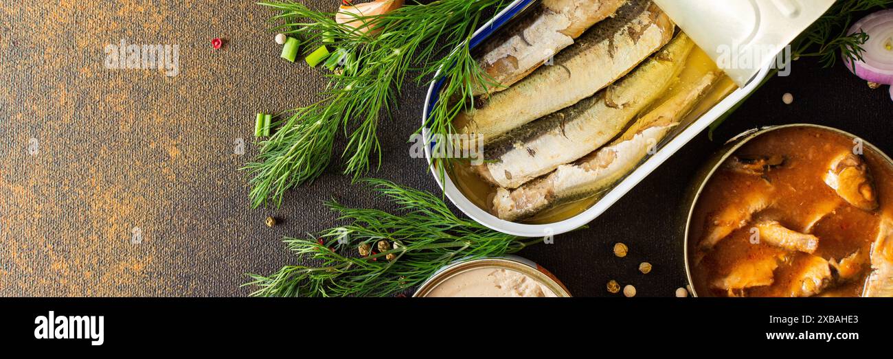 Different open tin cans with canned fish among spices and herbs banner ...