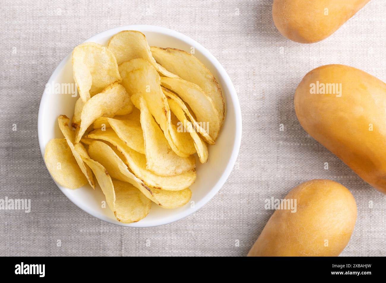 Salted potato chips in a white bowl on linen fabric. Crisps, slim ...