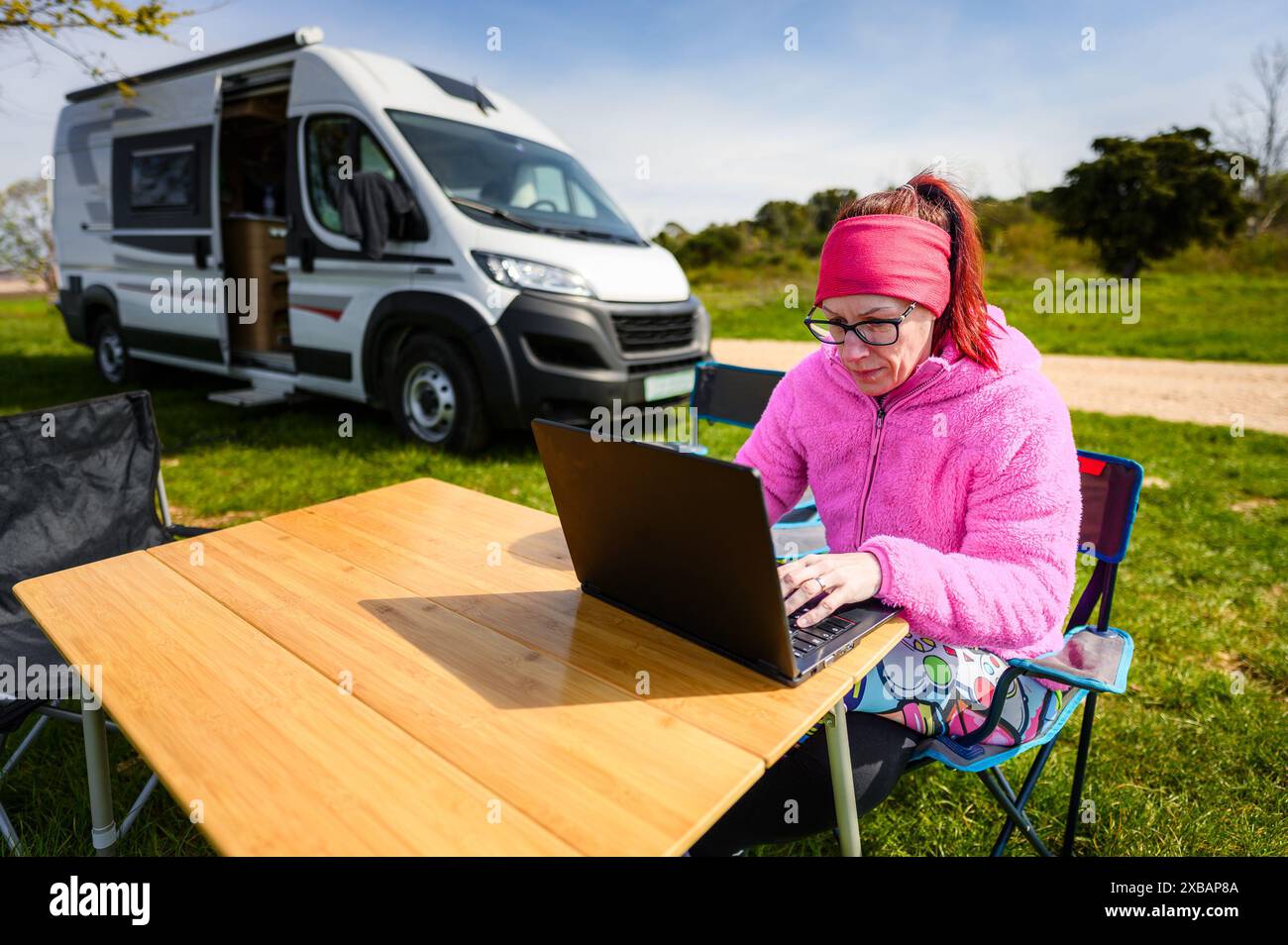 Woman freelancer working on laptop in front of campervan or motorhome ...