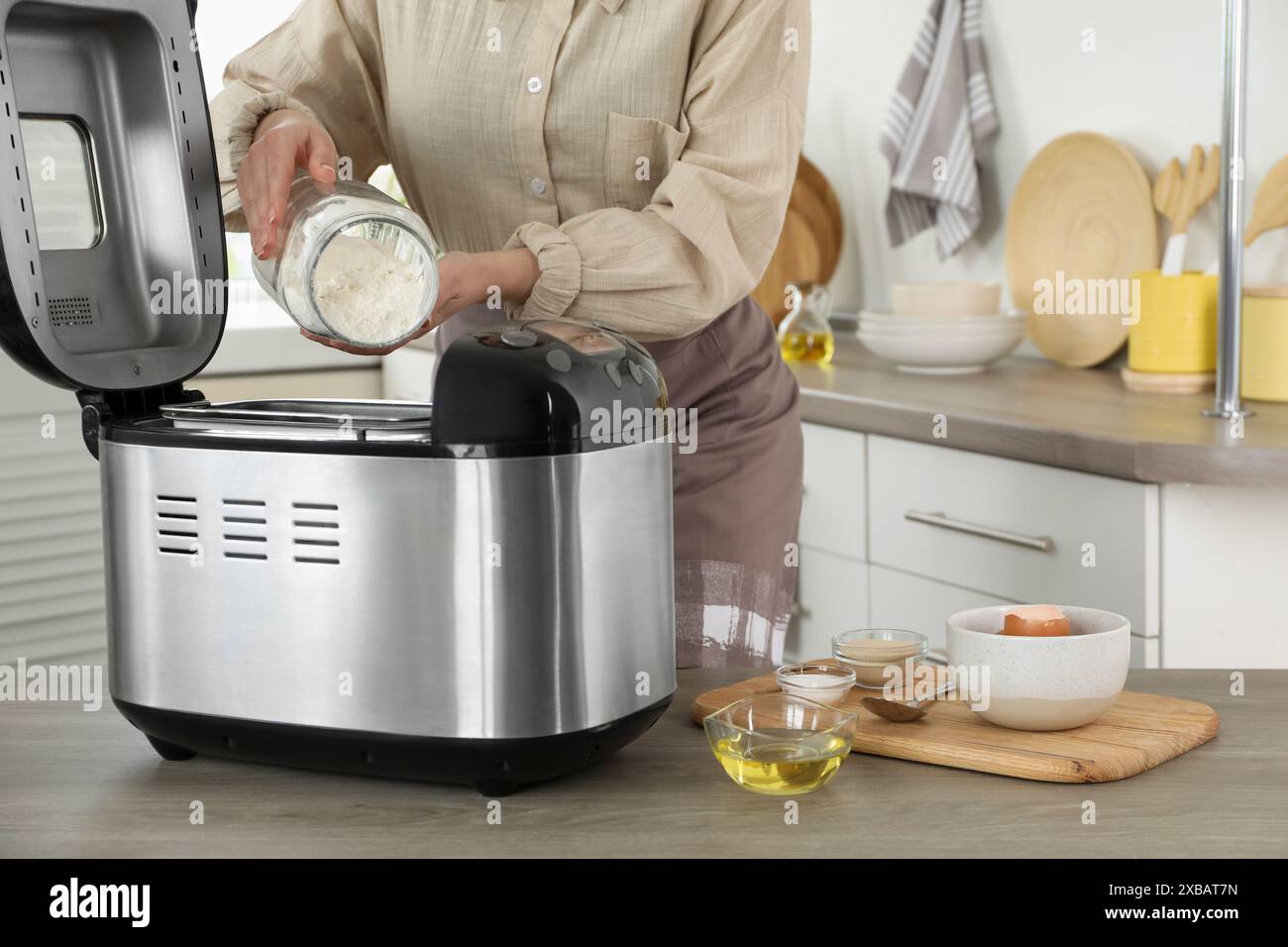 Making dough. Woman adding flour into breadmaker machine at wooden ...
