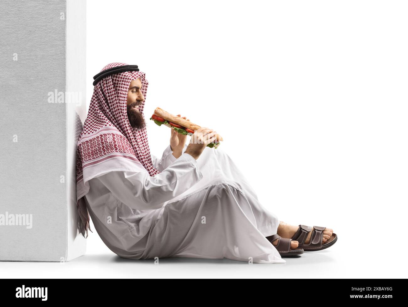 Saudi arab man sitting on the ground and eating a sandwich isolated on ...