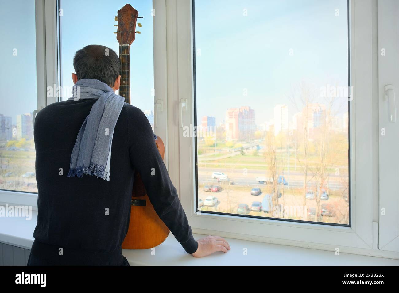 A man with a guitar in his hands is standing by the window. Musician ...