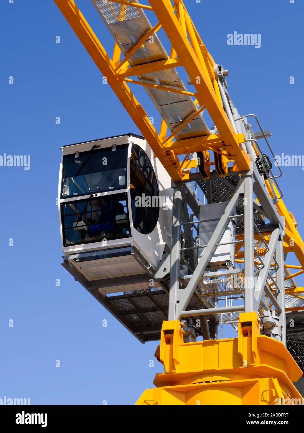 Construction tower crane cabin, isolated on clear blue sky background, low angle perspective ...