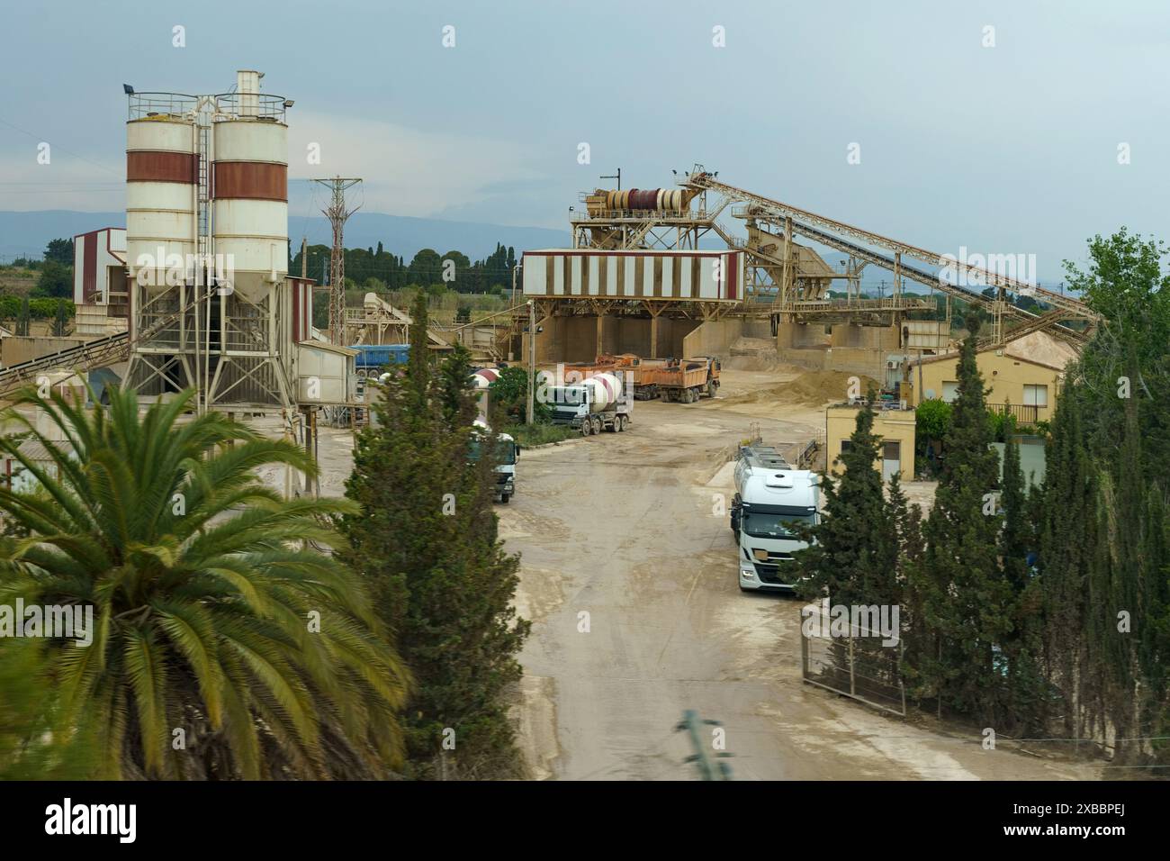 A truck is parked in front of a busy cement plant, ready for loading or ...